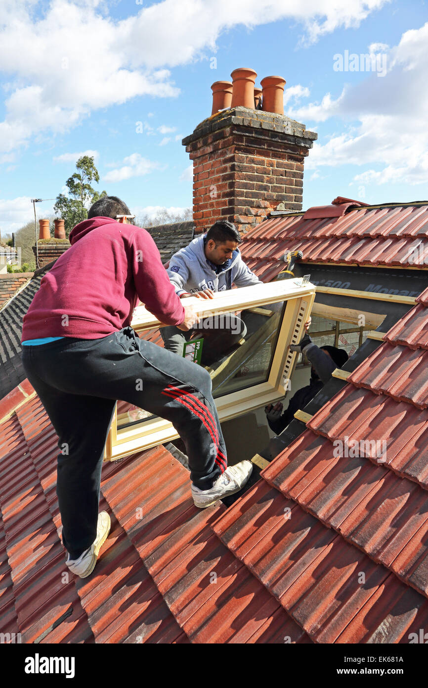 foreign builders installing a roof window on a pitched tiled roof in ...