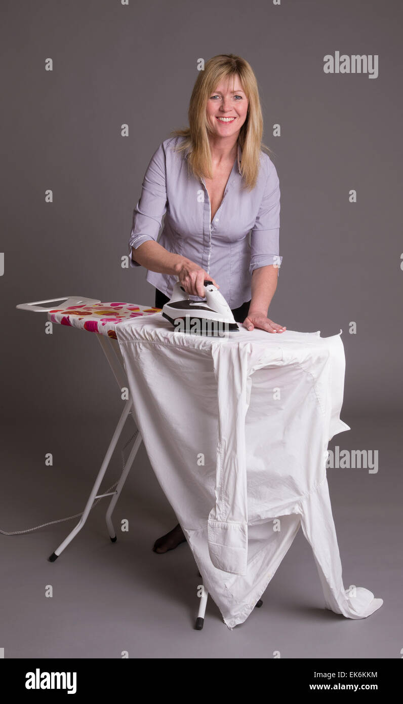 Woman standing at ironing board ironing a white shirt Stock Photo - Alamy
