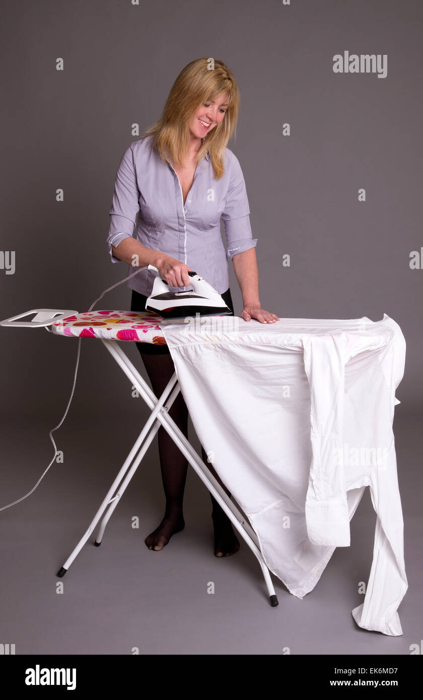 Woman standing at ironing board ironing a white shirt Stock Photo - Alamy