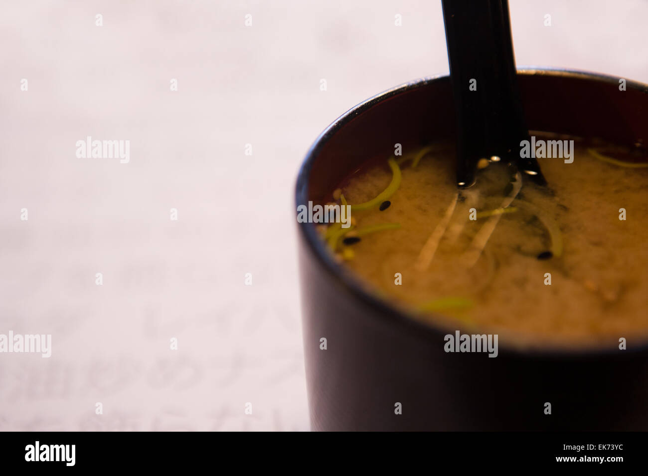 A close-up of a black and red bowl with delicious miso soup and spoon ...
