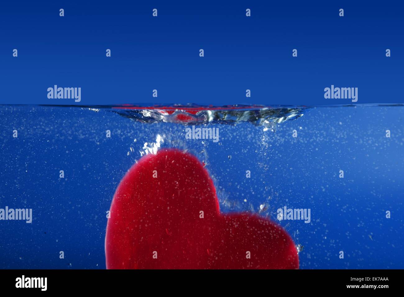 Candy red heart shape sinking into the blue water Stock Photo - Alamy