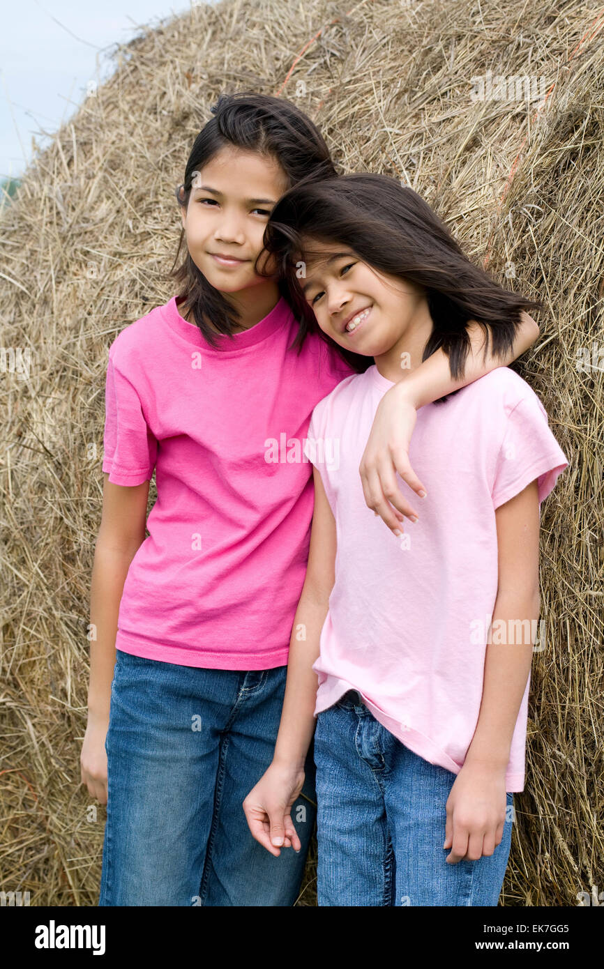 Two young girls standing against haybale Stock Photo - Alamy