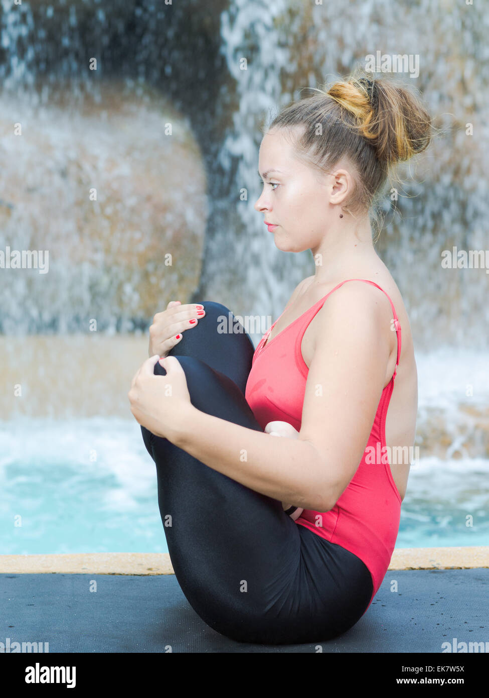 Woman practicing yoga near waterfall. Fetus Pose. Garbhasana Stock ...