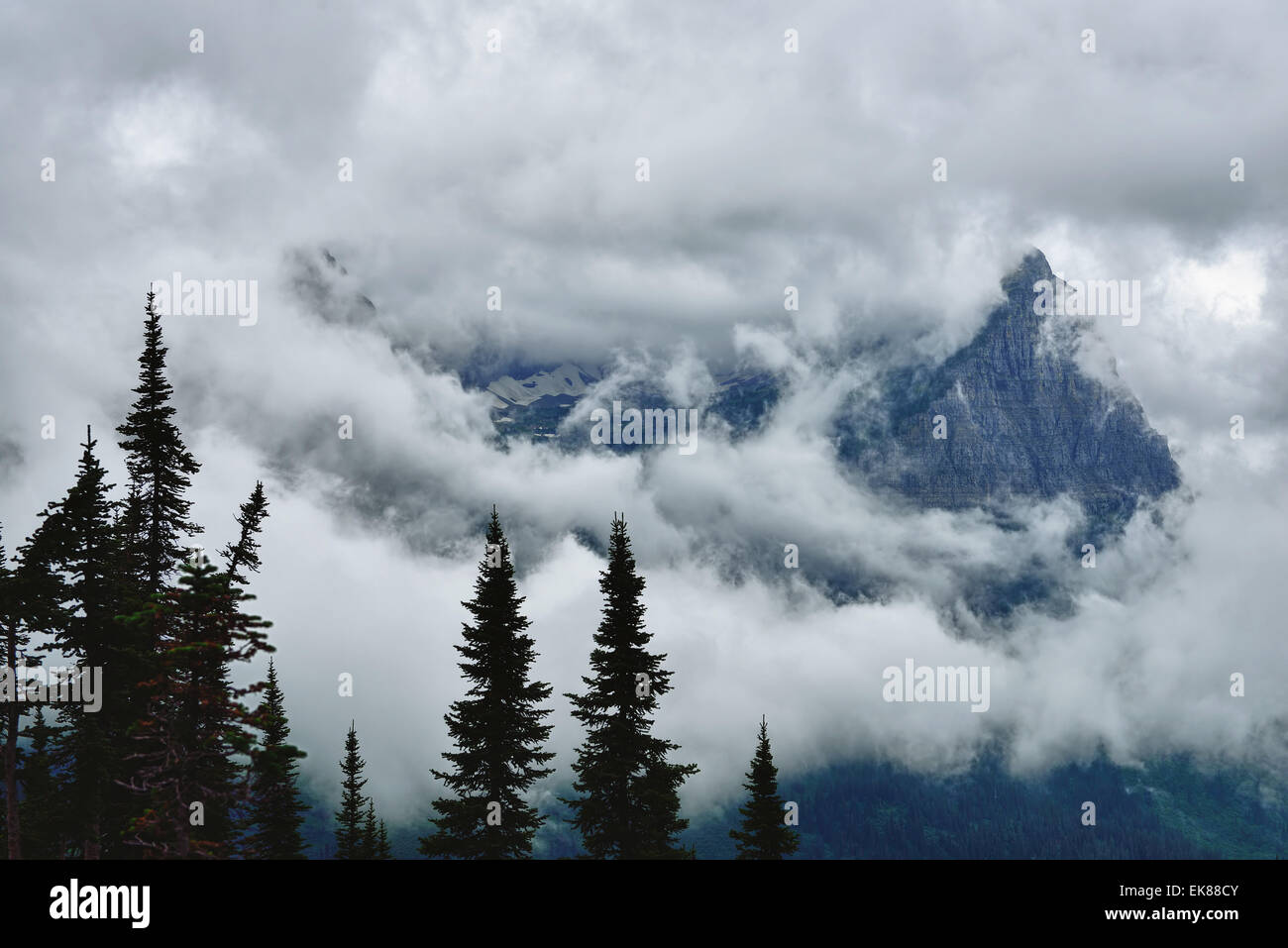high and steep mountain surrounded by heavy clouds in Glacier National ...