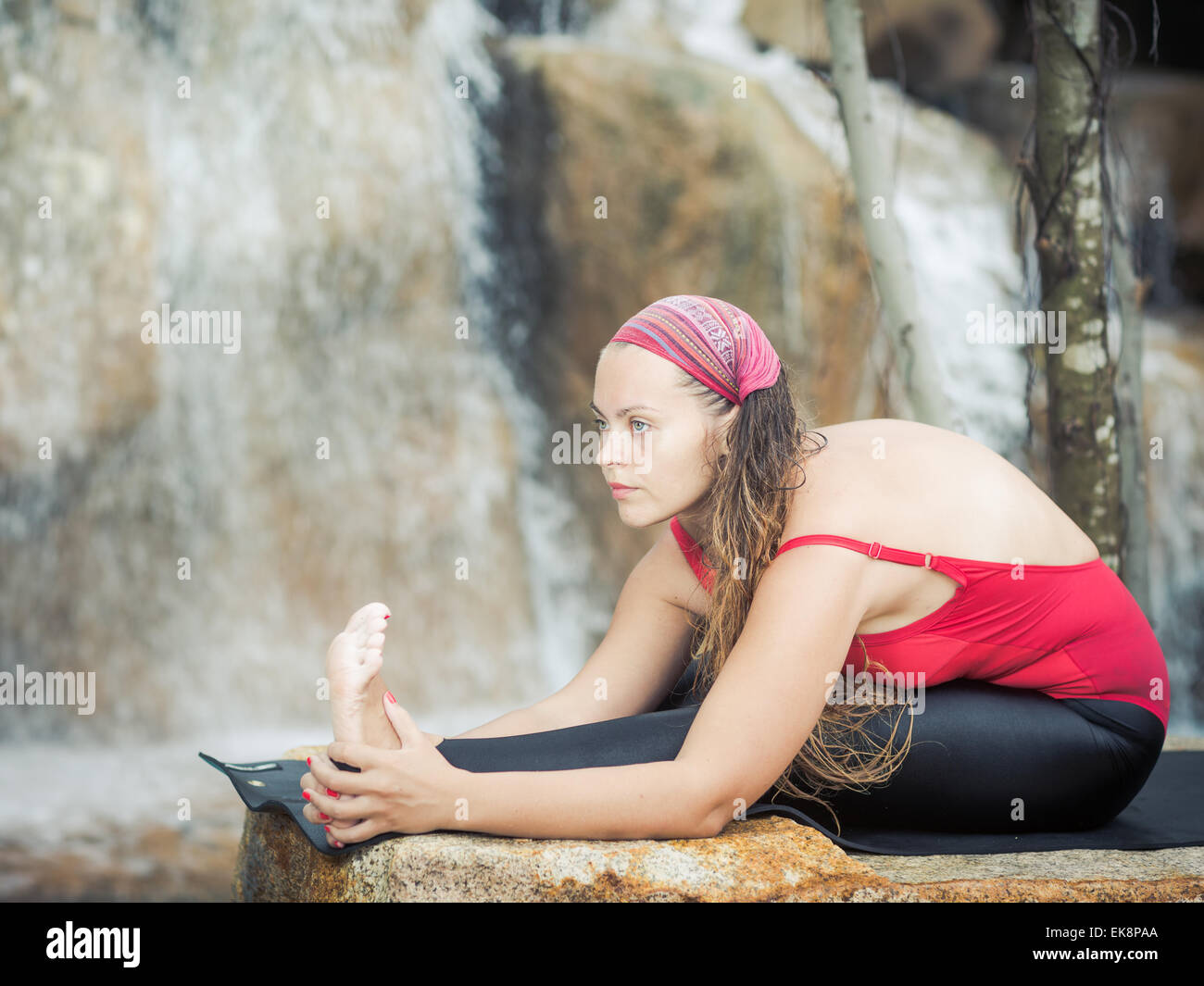 Woman practicing yoga near waterfall. Half hero stretch. Ardha Virasana ...