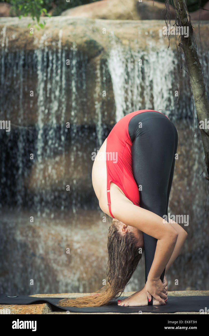 Woman practicing yoga near waterfall. Standing Forward Bend. Uttanasana ...