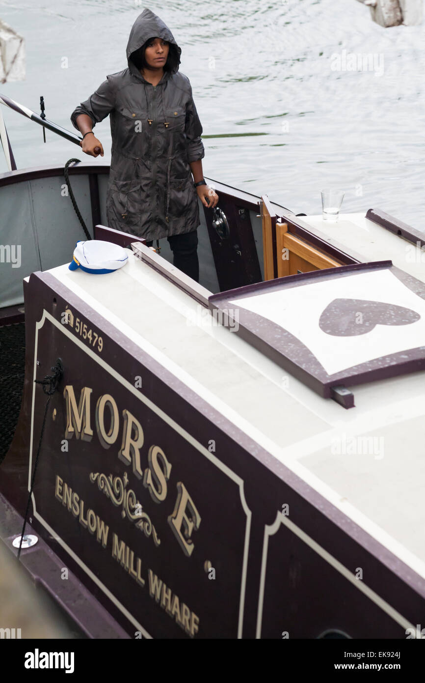Young woman steering Morse narrow boat narrowboat in the rain on the ...