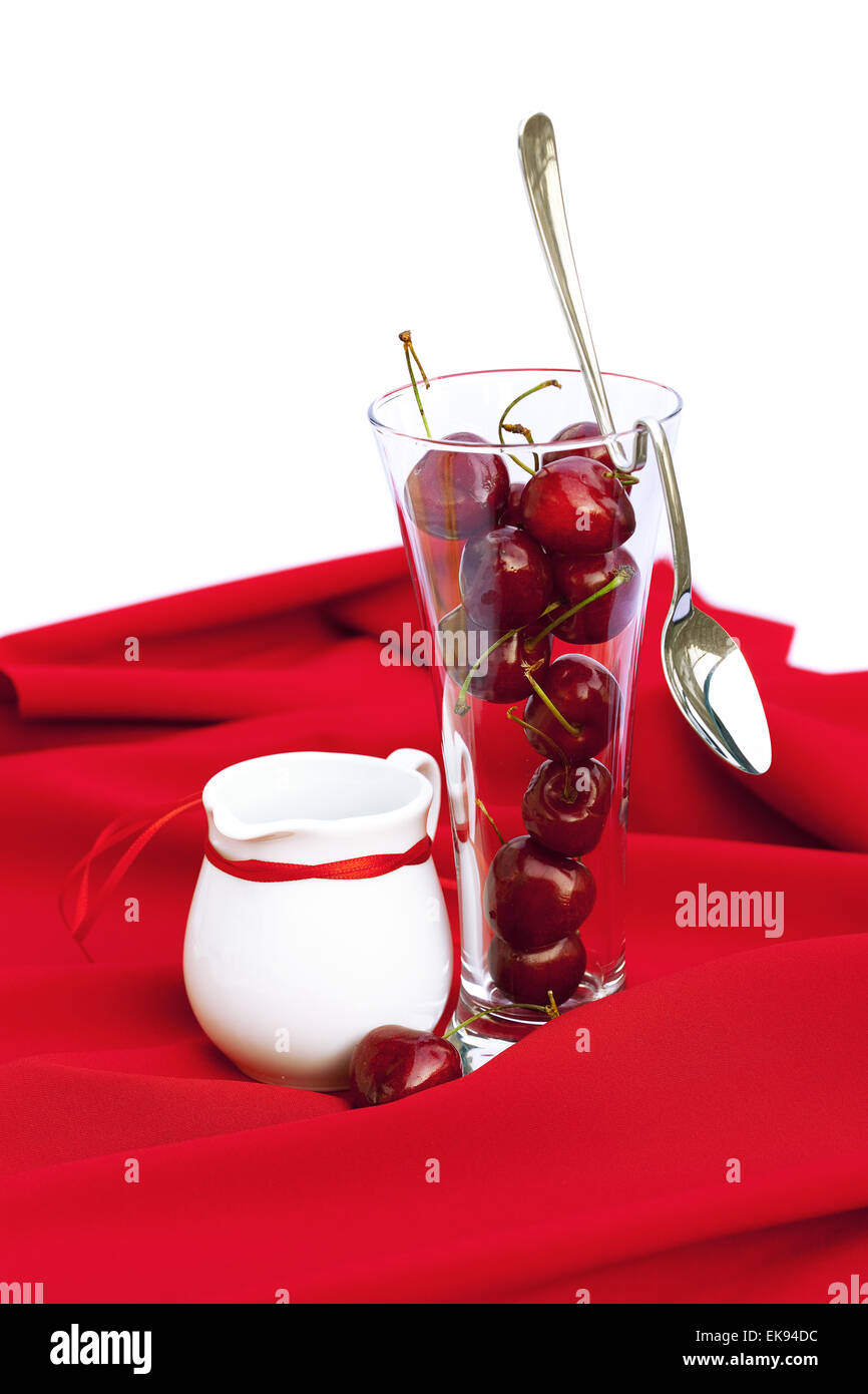 milk jug with a ribbon glass of cherry and spoon on a red backg Stock ...