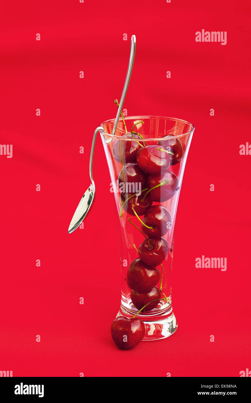 glass of cherry and spoon on a red background Stock Photo - Alamy