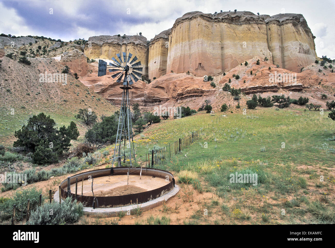 A windmill and water tank located at the base of a colorful sandstone ...