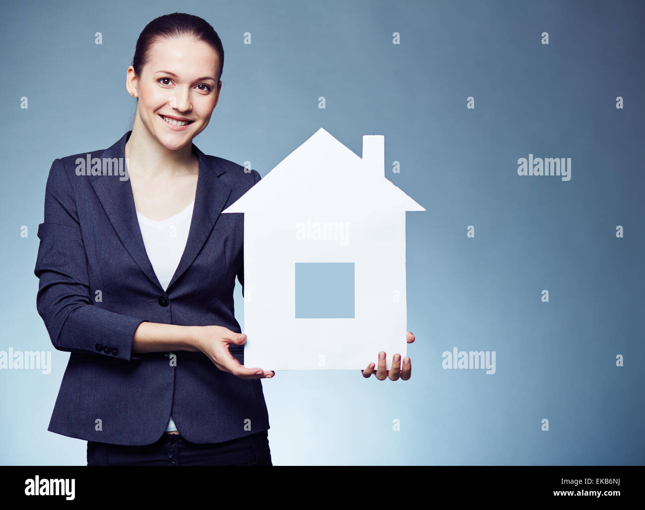 Cheerful female realtor showing paper house Stock Photo - Alamy