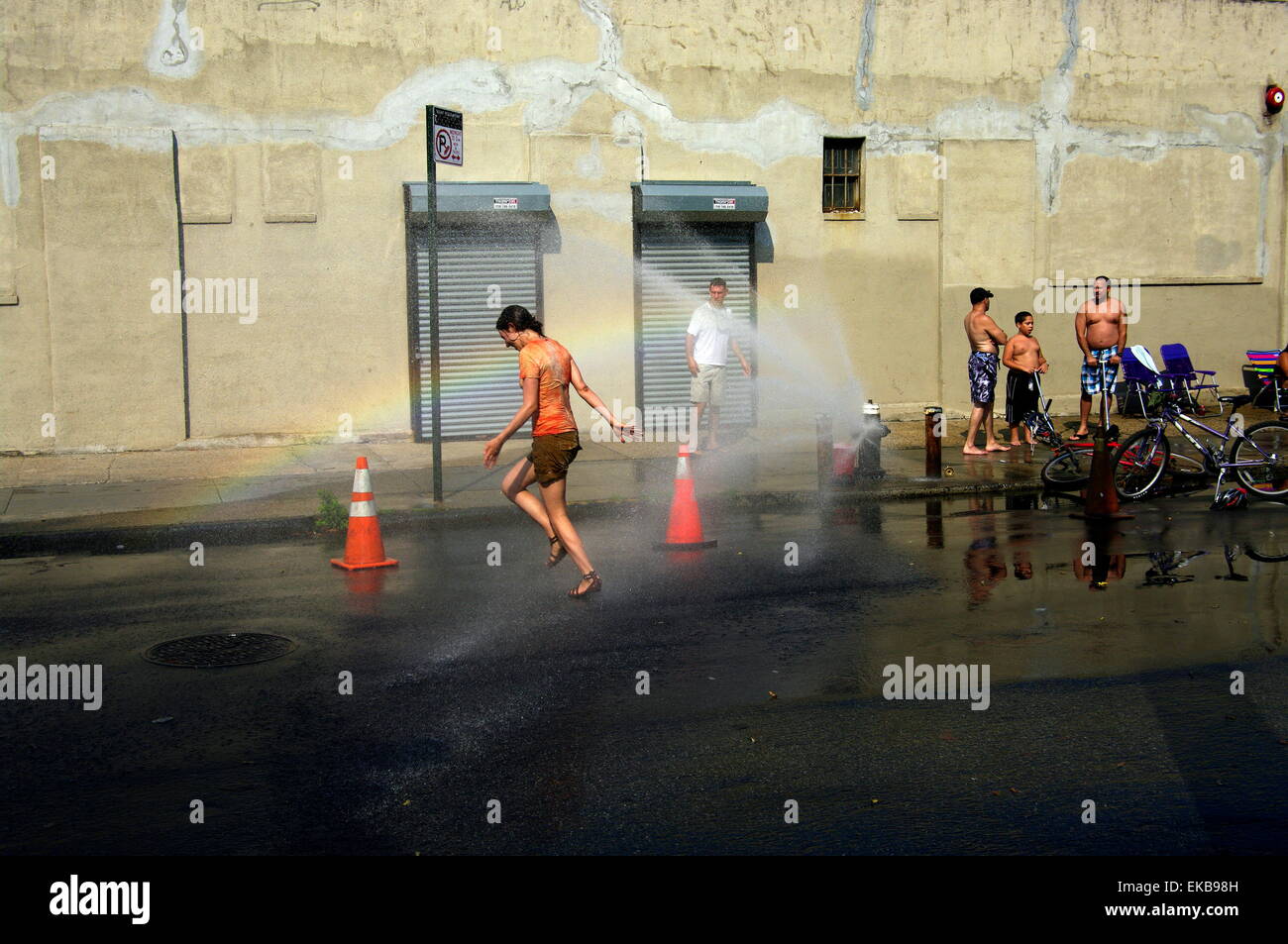 Summer street scene in Brooklyn, girl playing in open fire hydrant with ...