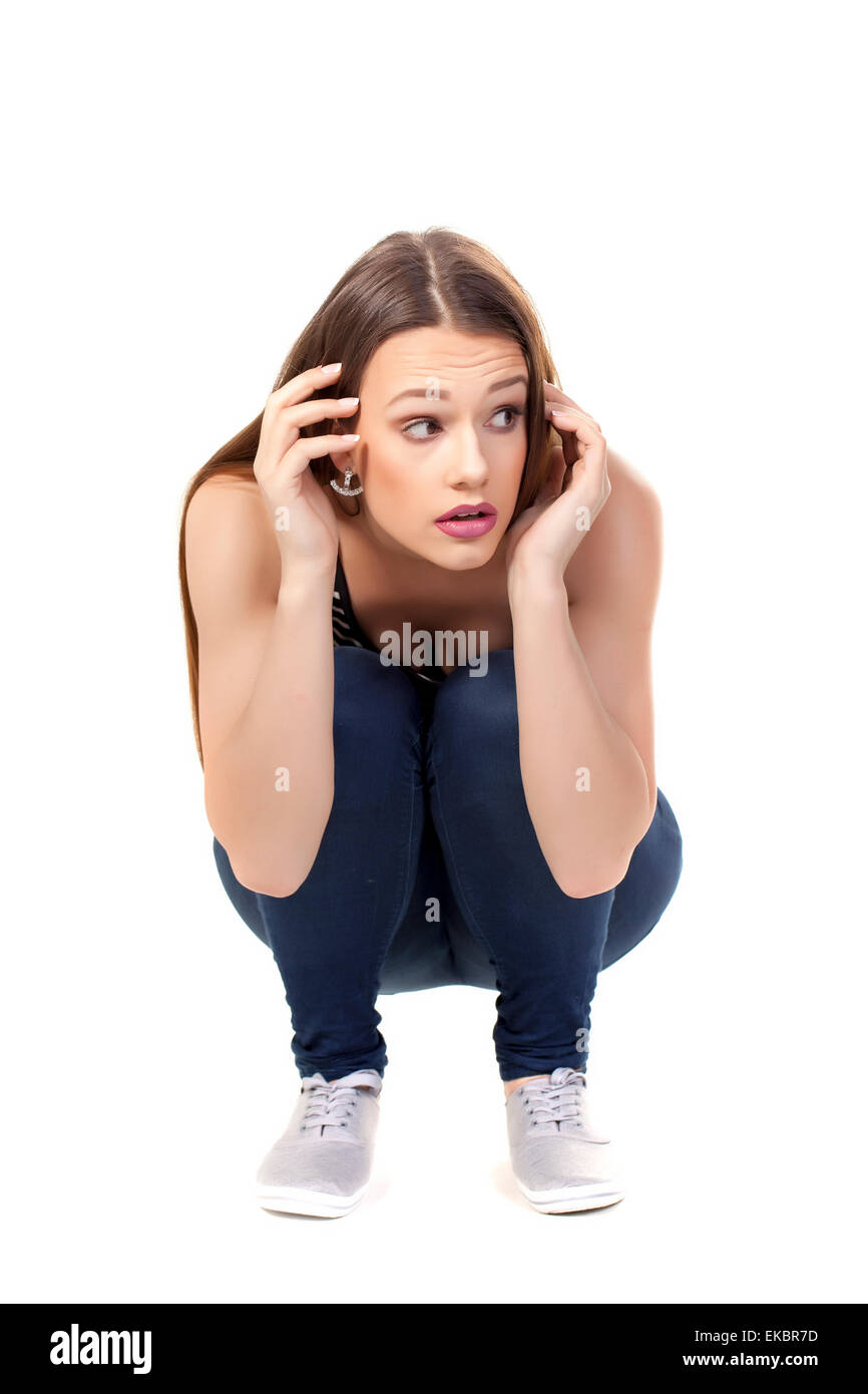 Expressive young woman crouching down in fear over a white background ...