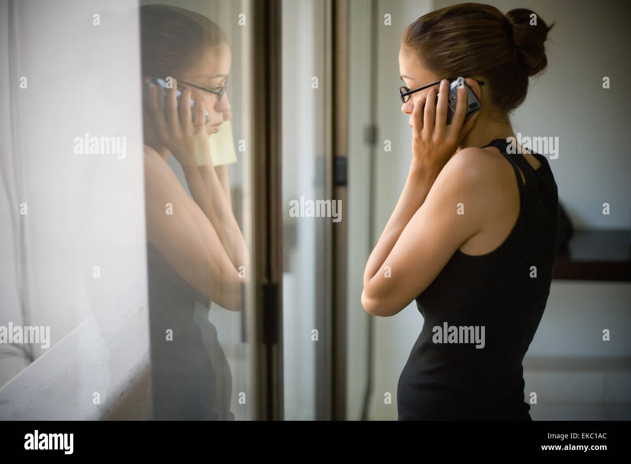 Woman standing by window, holding mobile phone to ear Stock Photo - Alamy