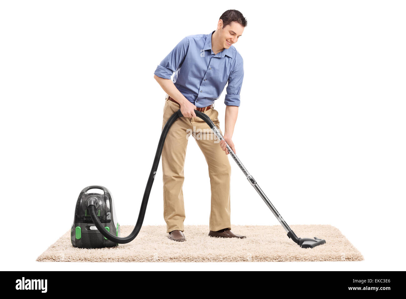 Full length portrait of a young man cleaning a carpet with a vacuum ...