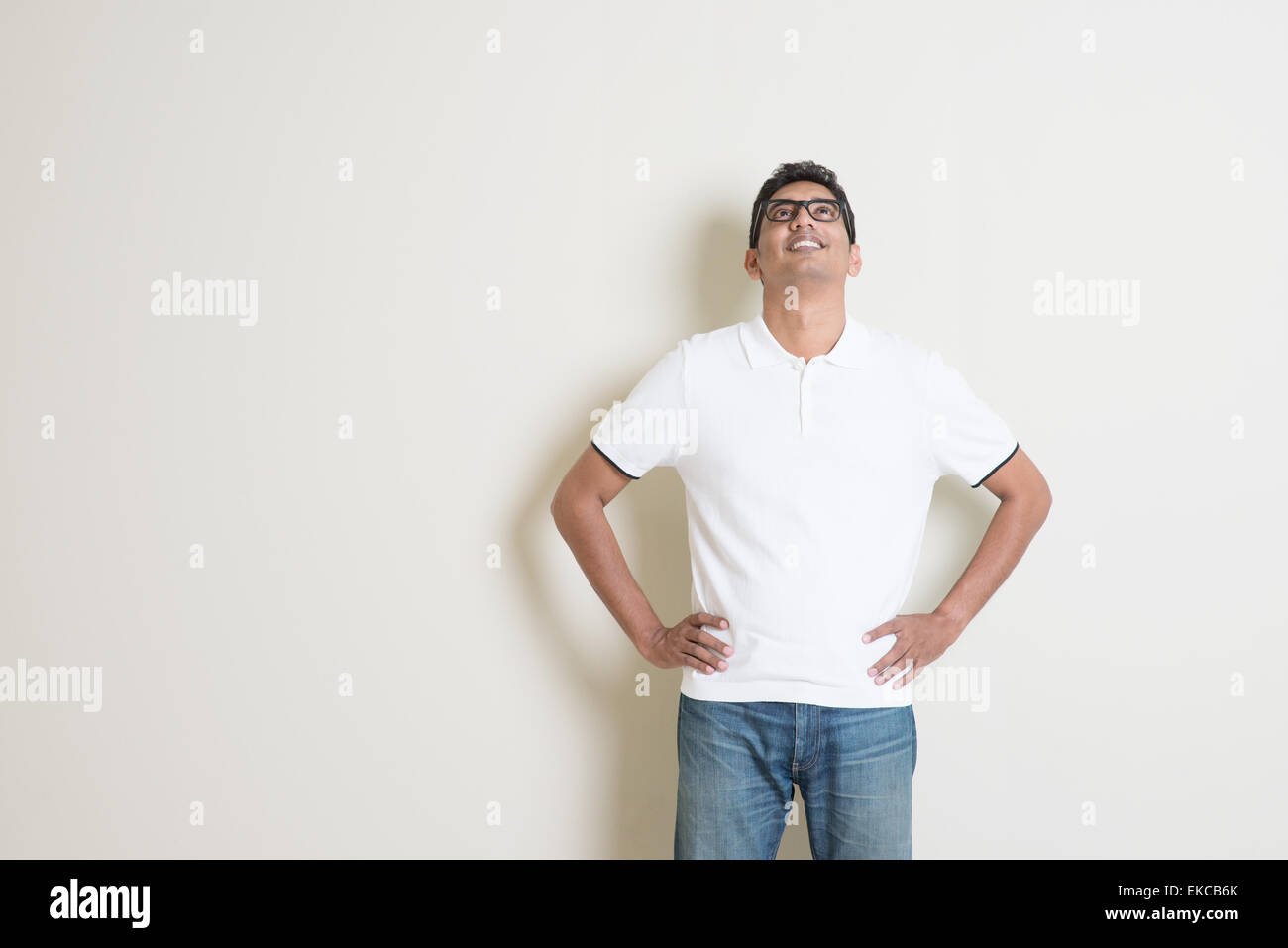 Portrait of handsome Indian guy looking up, standing on plain ...