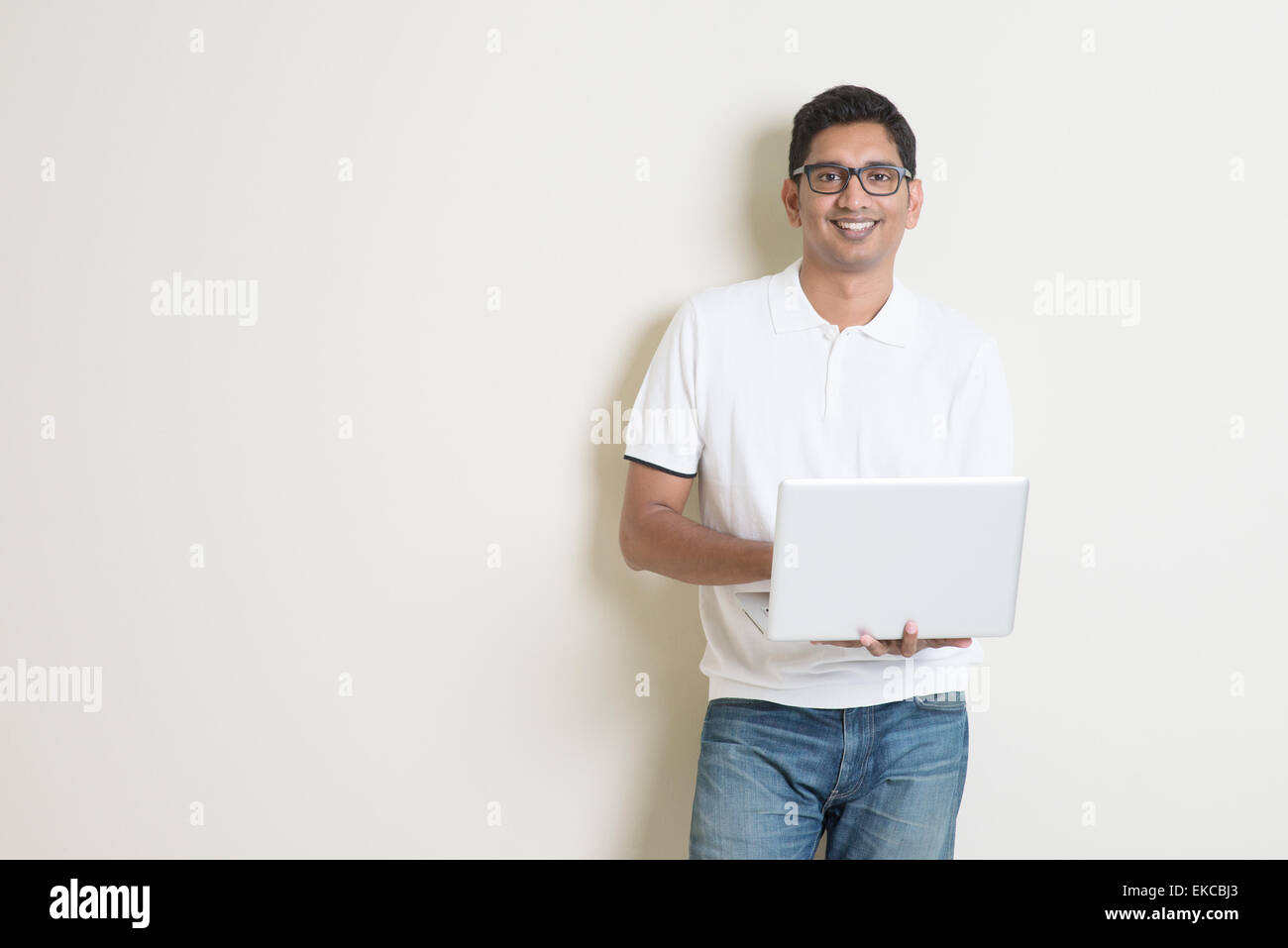 Portrait of handsome Indian guy using laptop computer, standing on ...