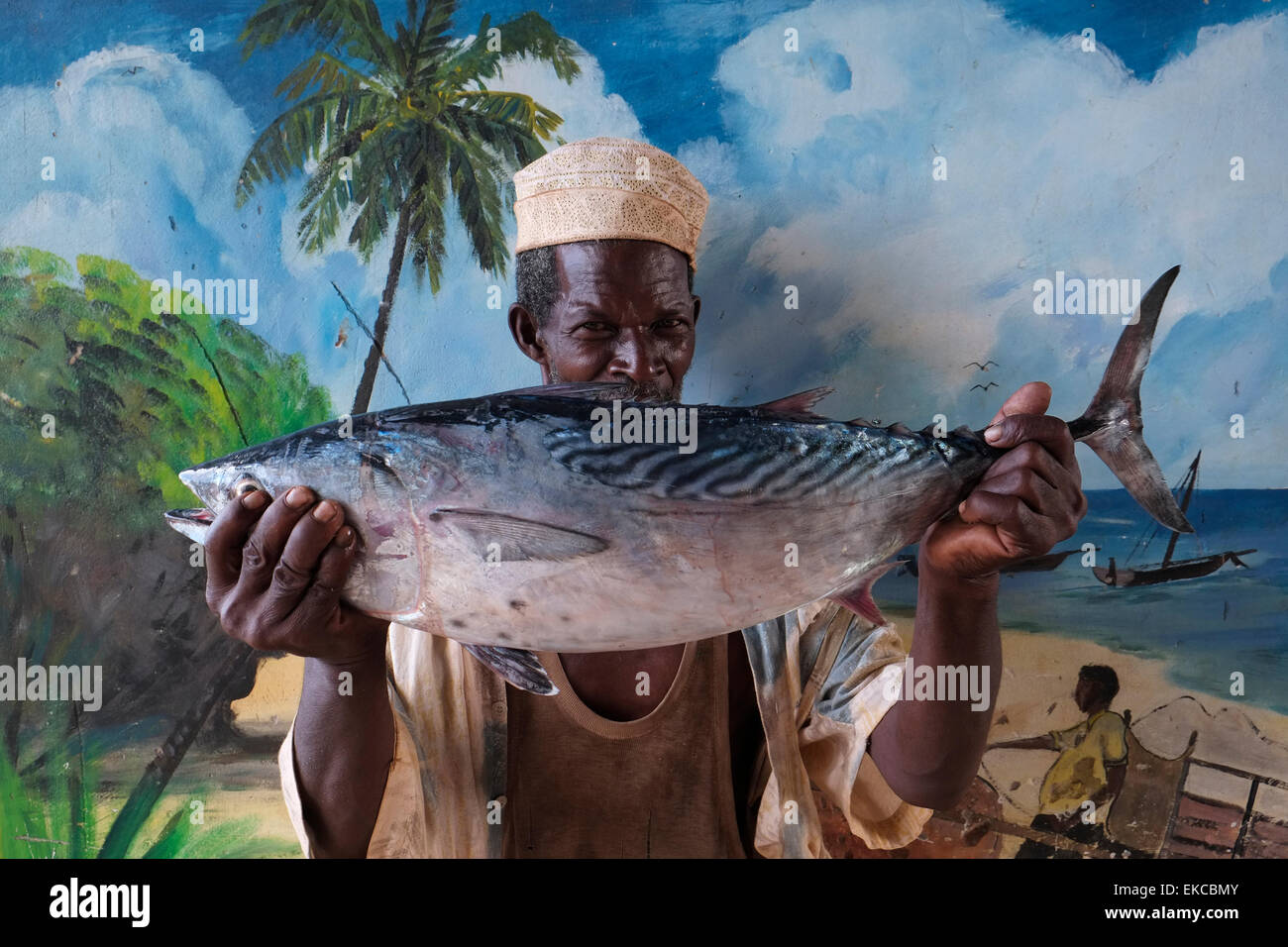 A fishmonger holds a Tuna fish as he stands next to a painted wall in ...