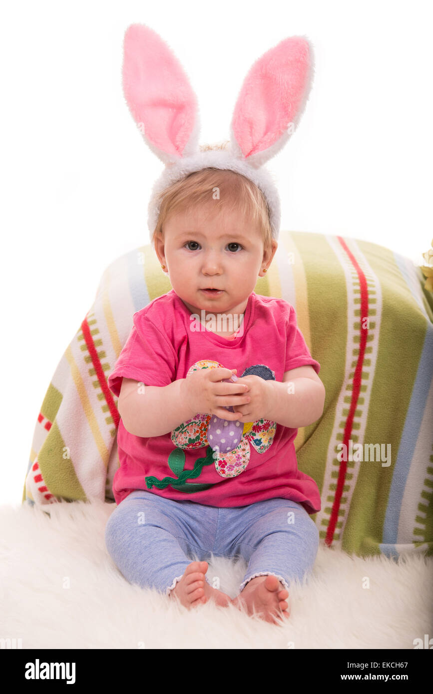 Cheerful baby girl with bunny ears holding lilla Easter egg and sitting ...