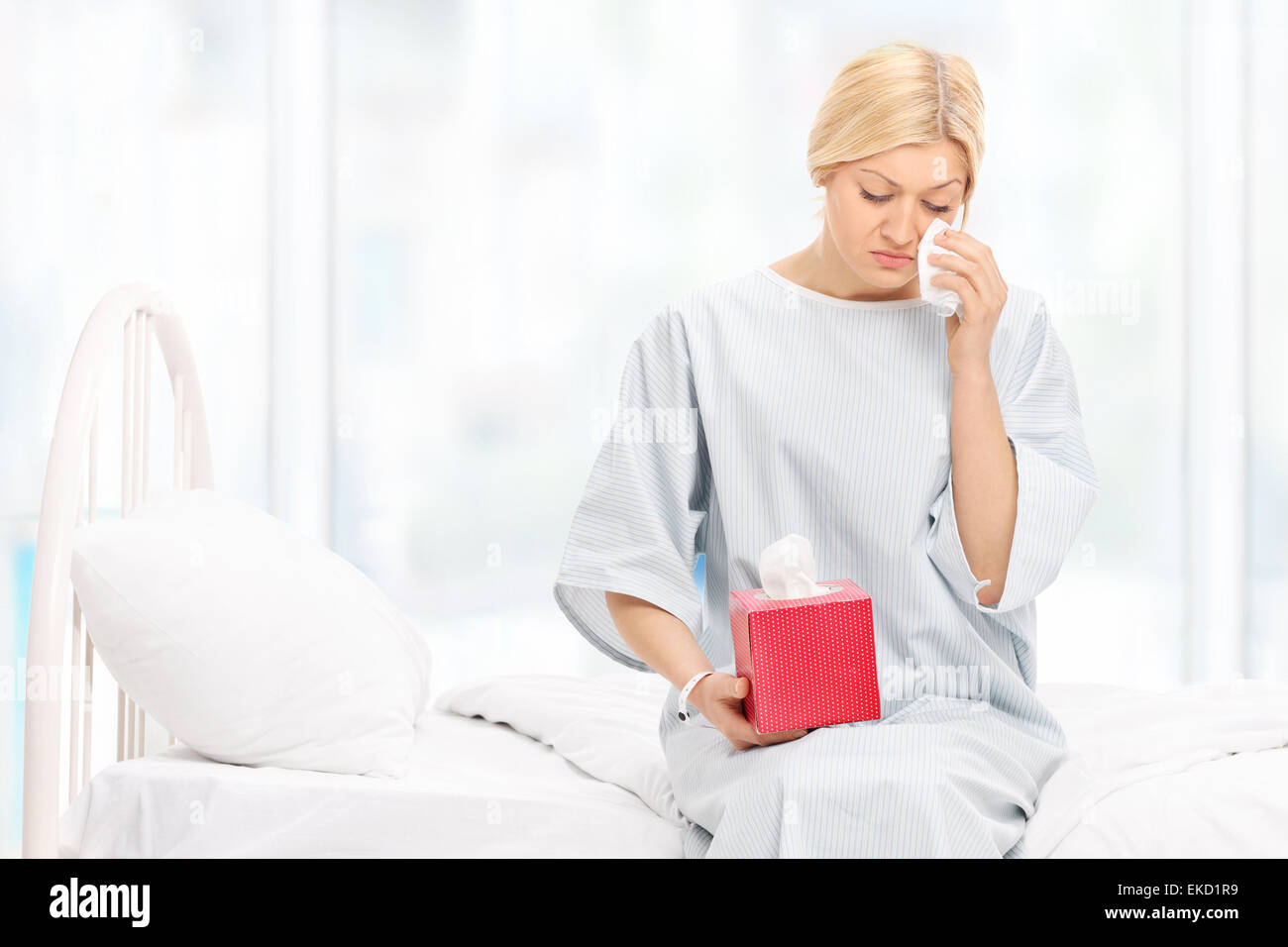Sad woman in a hospital gown crying and wiping her tears seated on a ...