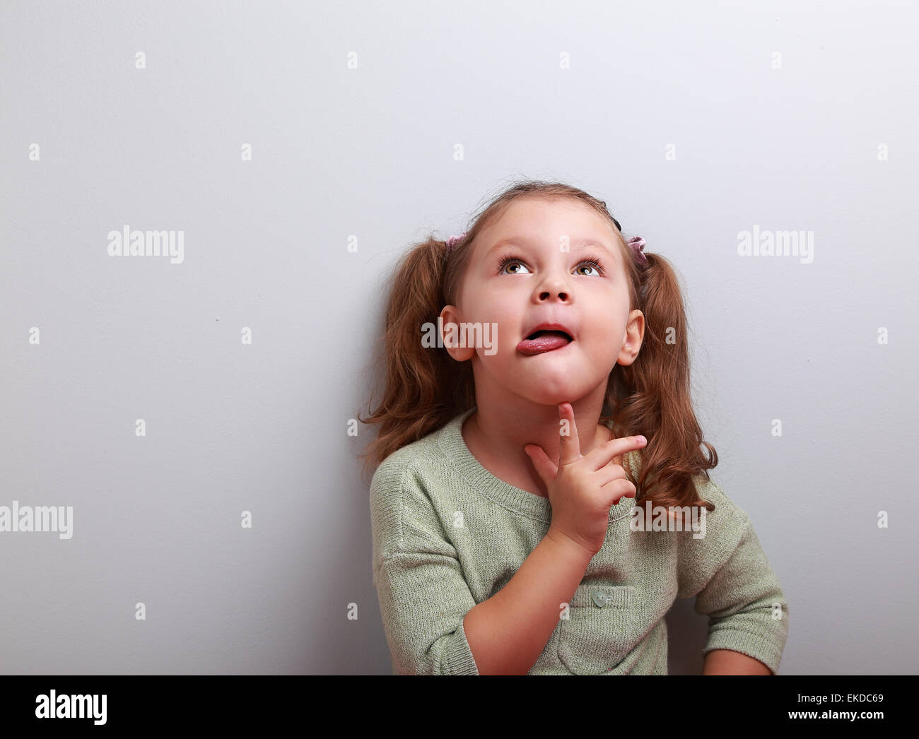 Thinking small kid showing the tongue looking up on empty copy space ...