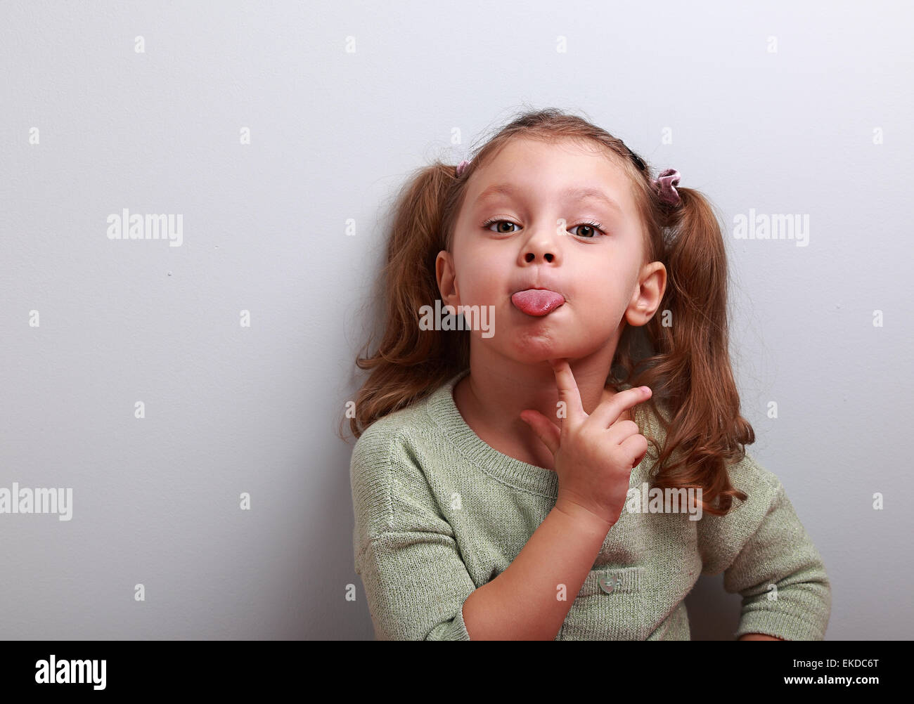 Thinking grimacing girl showing tongue with finger under face and ...
