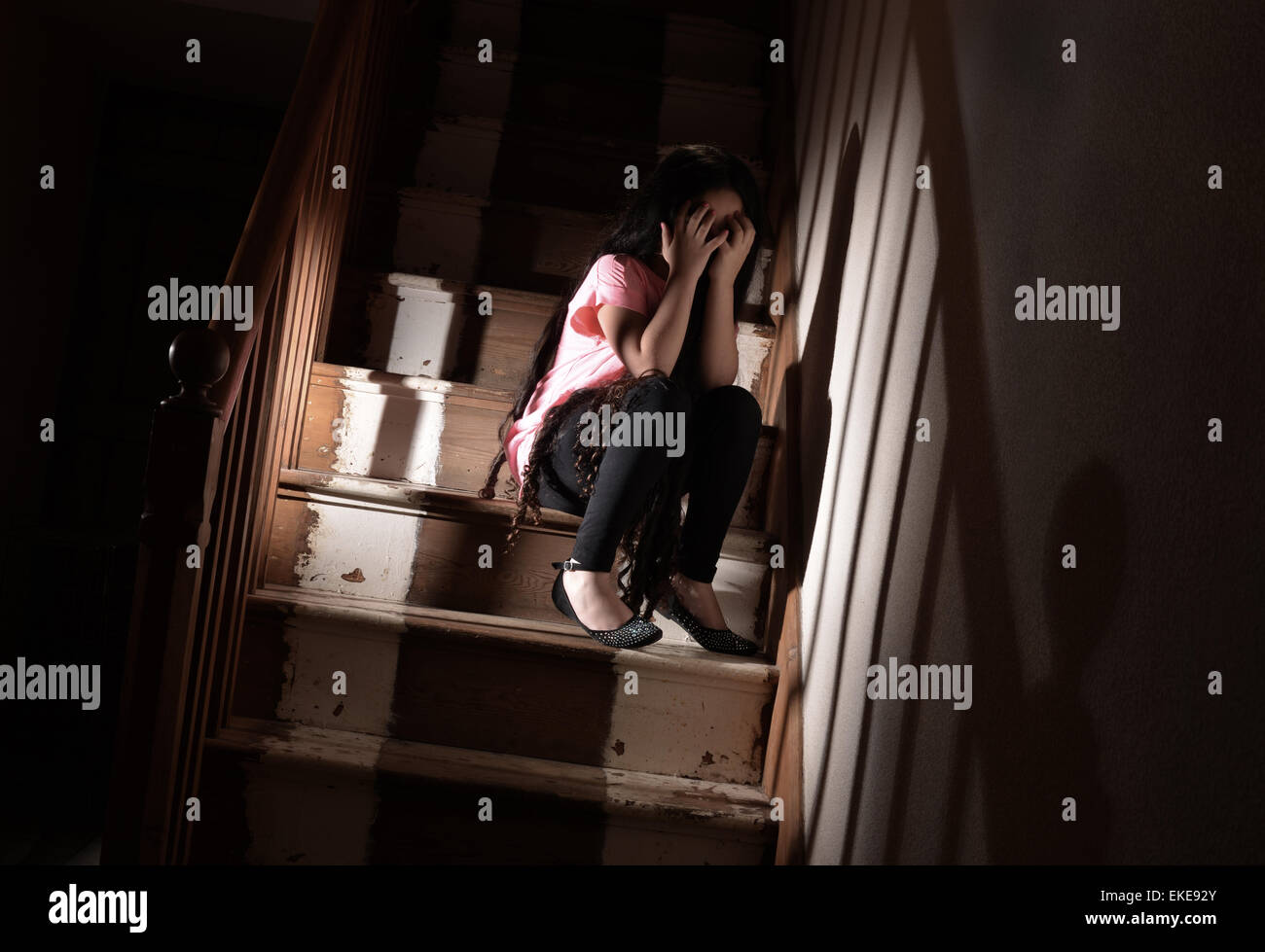 A young child crying on the stairs at home after suffering abuse. Posed ...