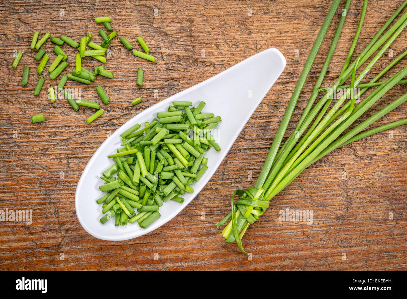 a spoon of chopped fresh chives with a bunch against rustic wood, top ...