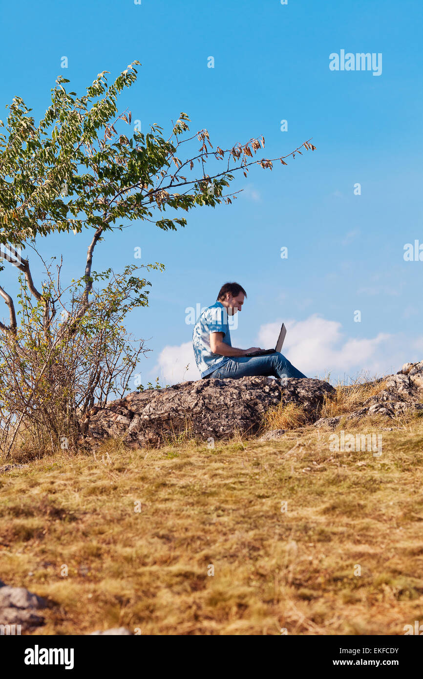 young man using laptop sitting on a hill against the blue sky Stock ...