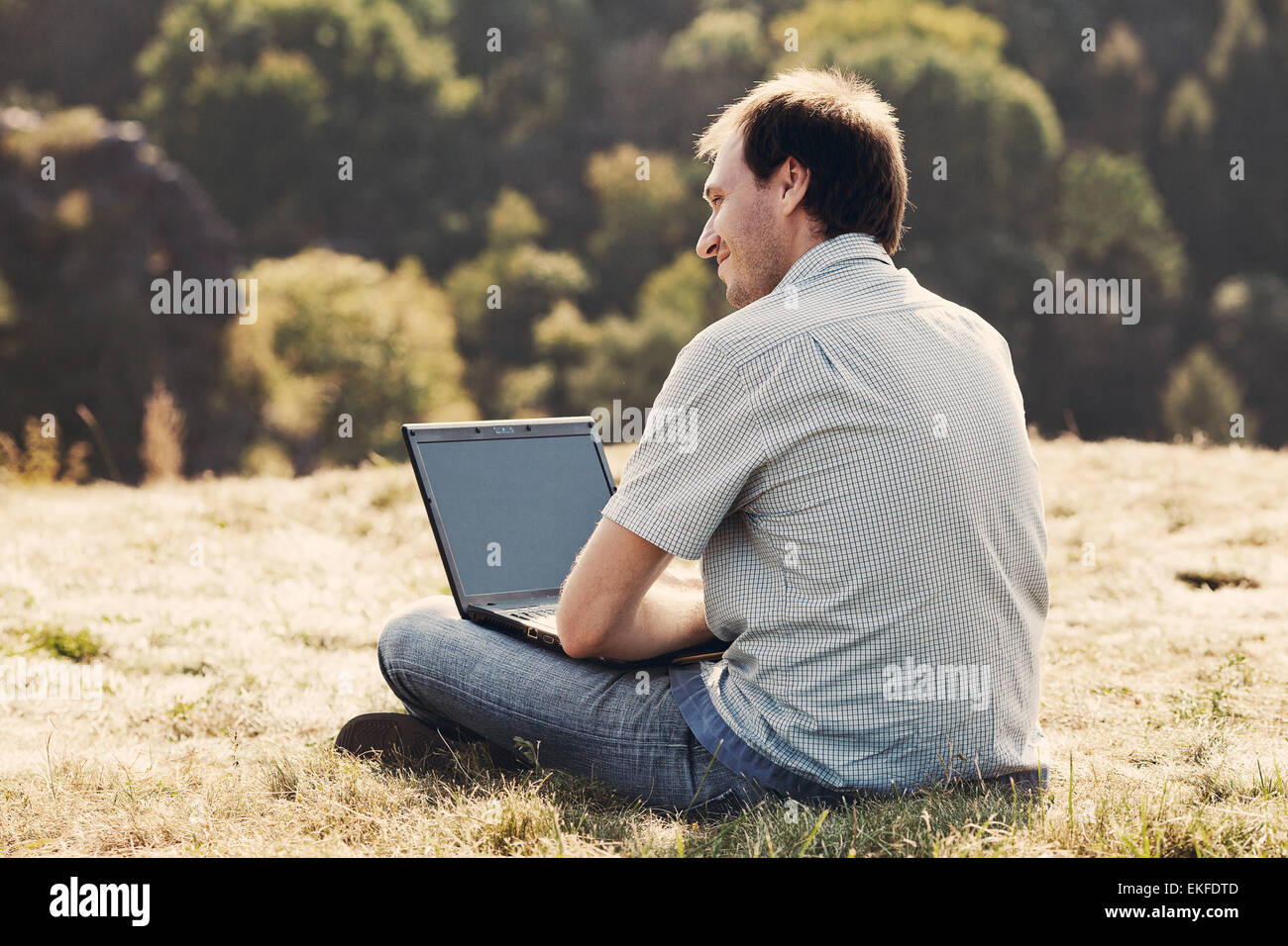 young man using laptop sitting on the grass on the hillside Stock Photo ...