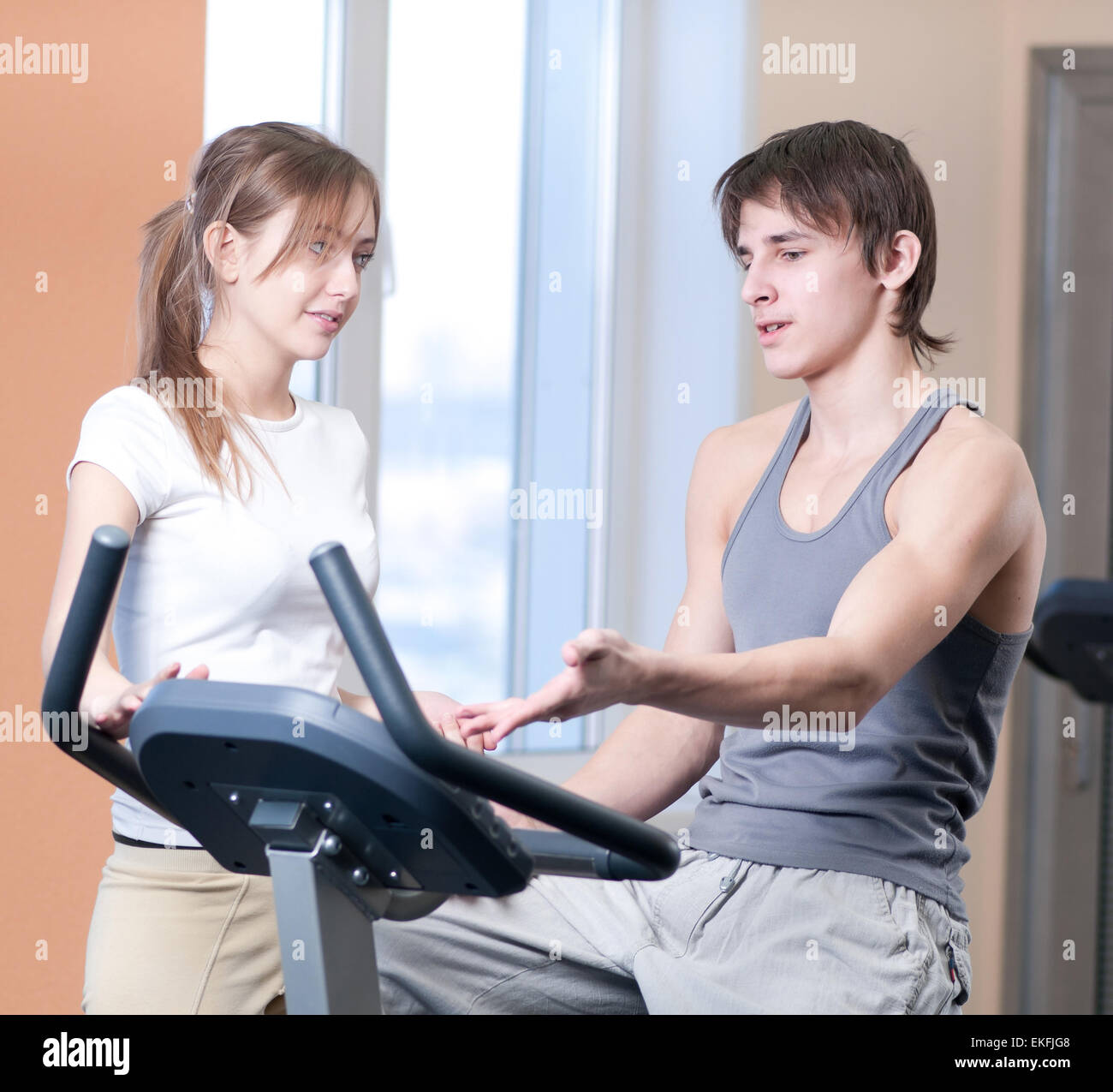 Train on machine in a gym assisted by personal instructor Stock Photo ...