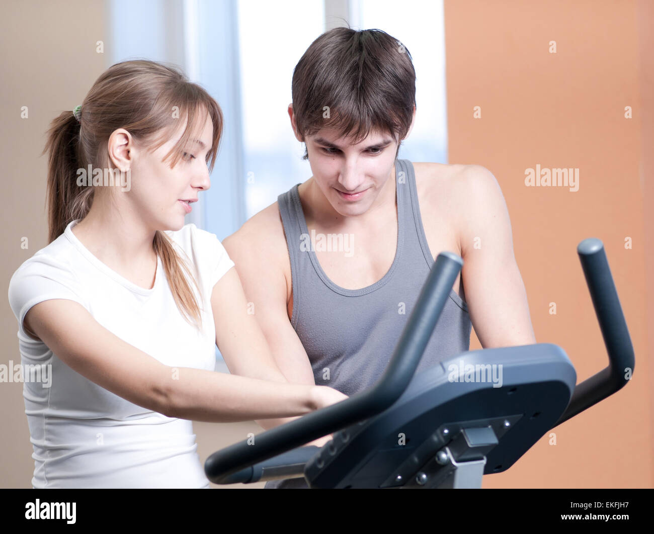 Train on machine in a gym assisted by personal instructor Stock Photo ...