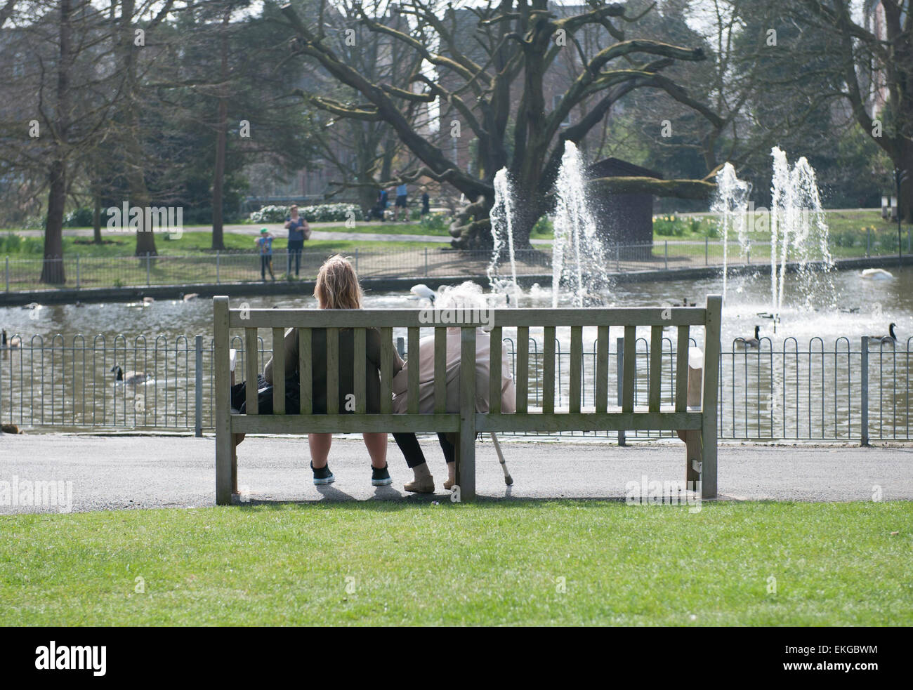 A younger woman and an elderly woman sit side by side on a park bench ...