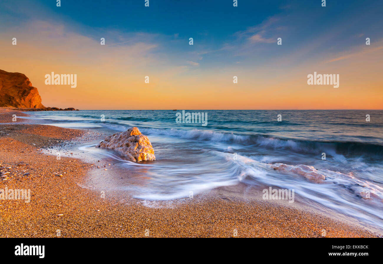 The sun sets illuminating the wet rocks and pebble beaches of the ...