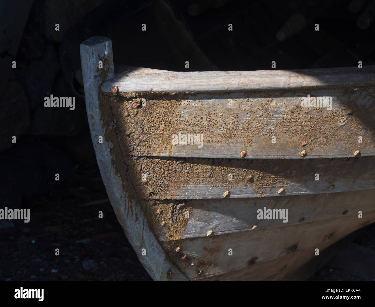 The prow of an old wooden rowing boat in the shadow of a boathouse ...