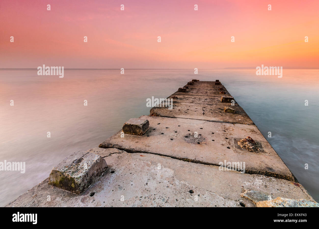A concrete and stone jetty reaches out to the sunset sky through calm ...