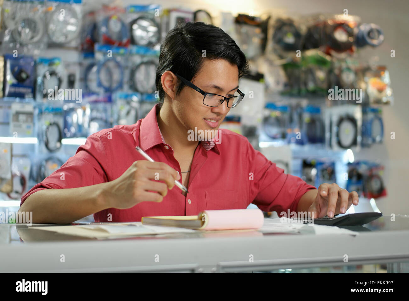Young asian entrepreneur owning a computer shop and checking bills and ...