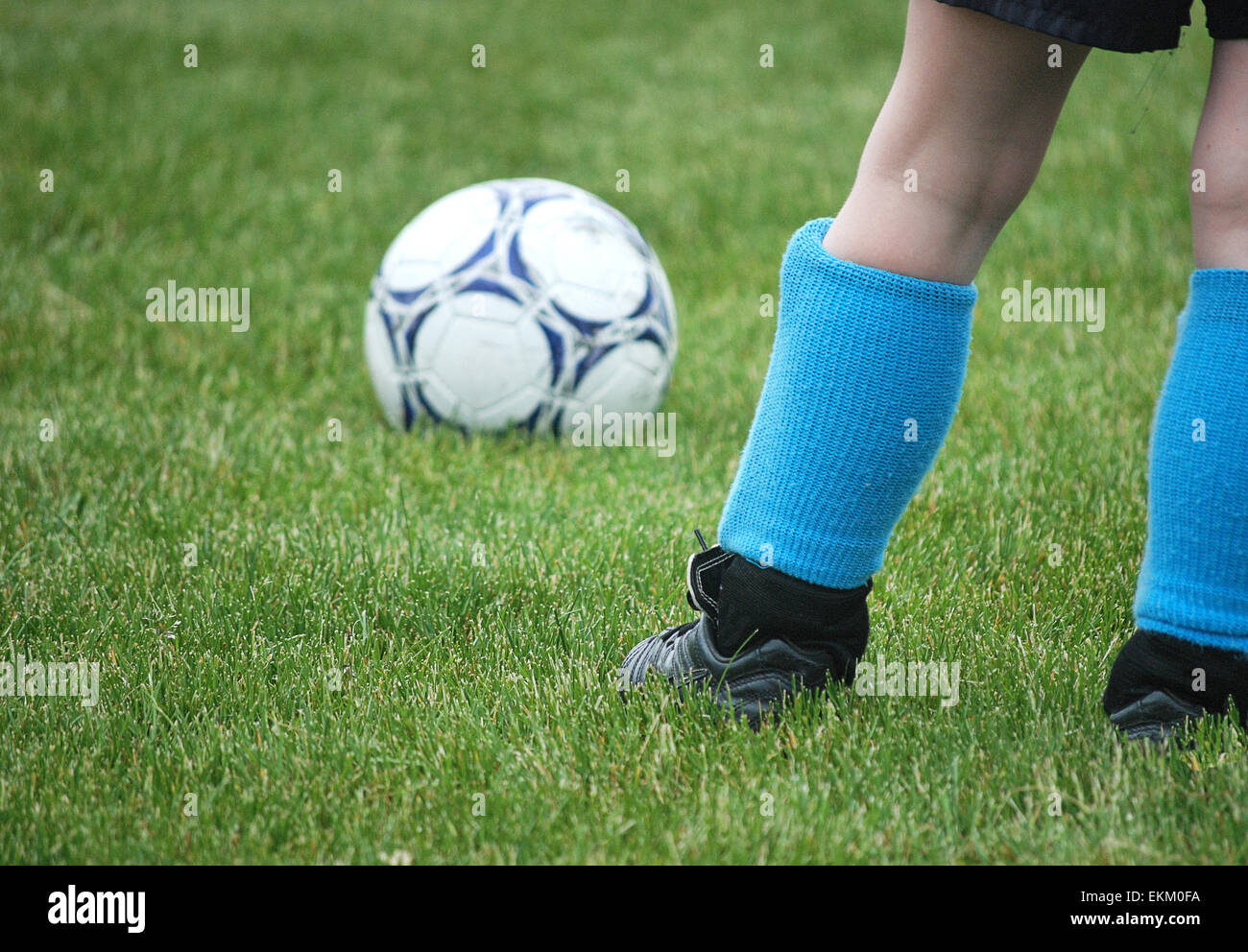 Young soccer player with blue socks and ball on grass Stock Photo - Alamy