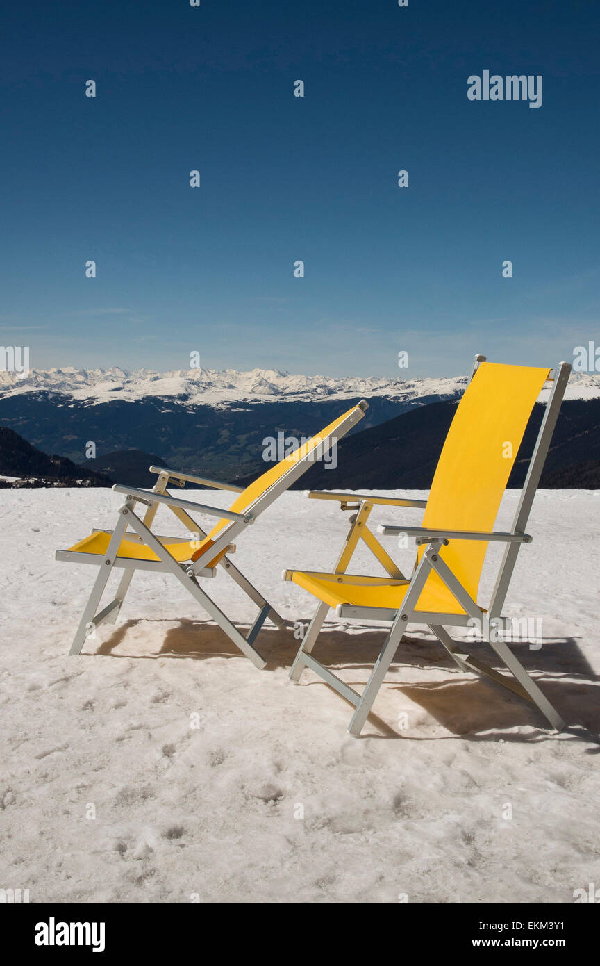 Yellow deck chairs on snow mountain top with snow covered mountains ...