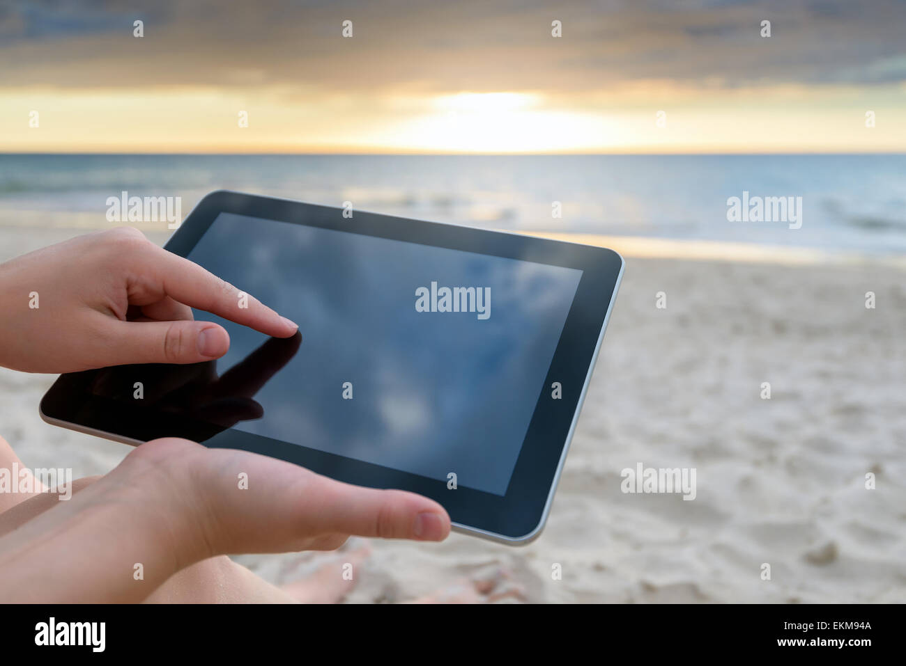 Woman holding a tablet at the beach during a warm sunset Stock Photo ...