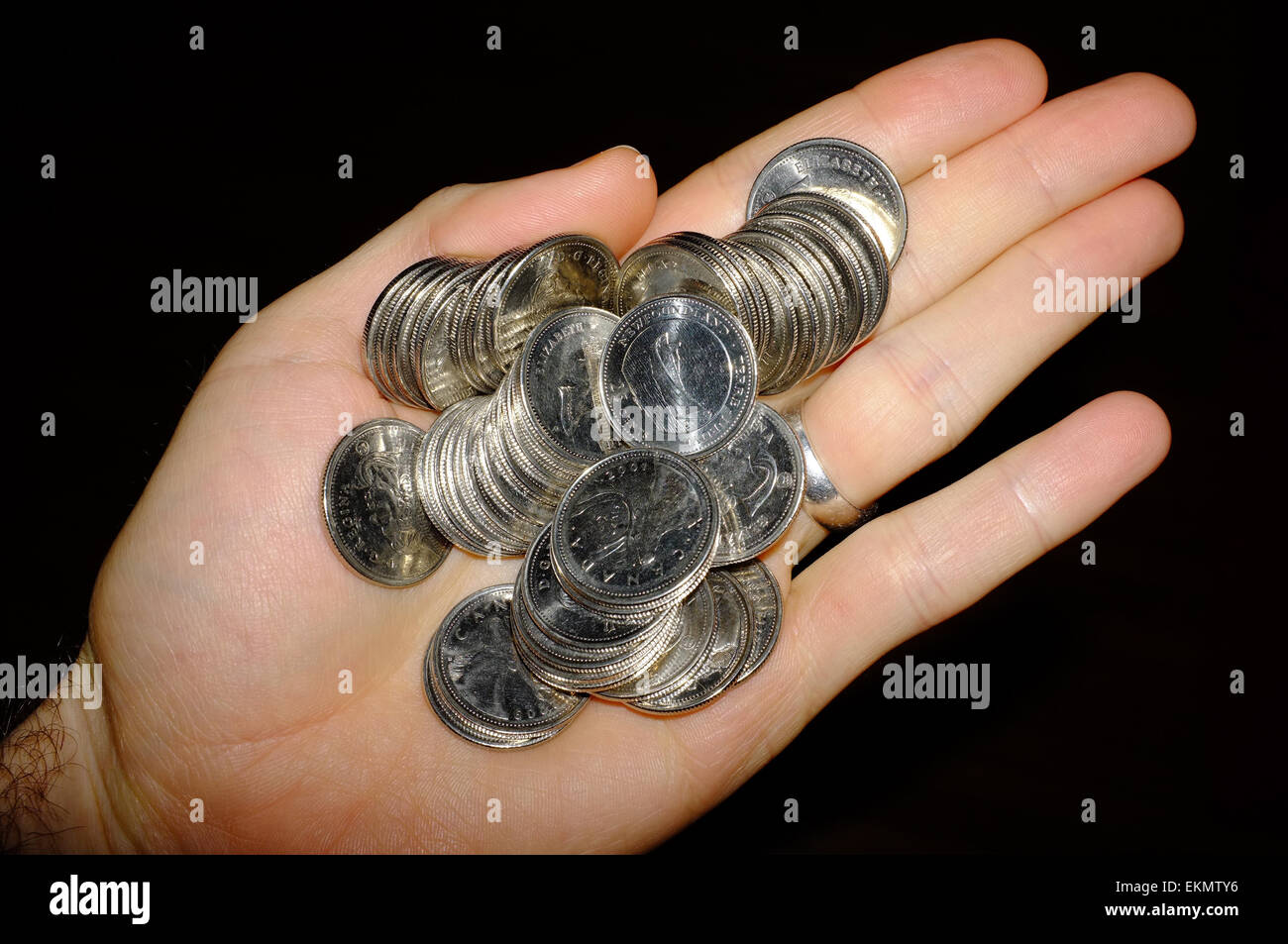 Image of a hand holding Canadian quarters against a black background ...