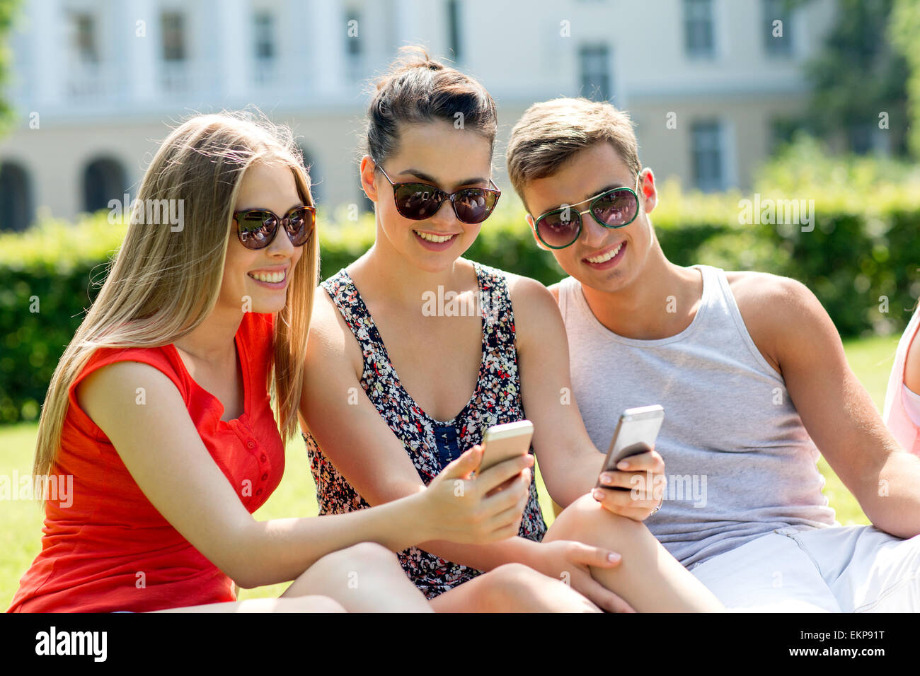 smiling friends with smartphones sitting in park Stock Photo - Alamy