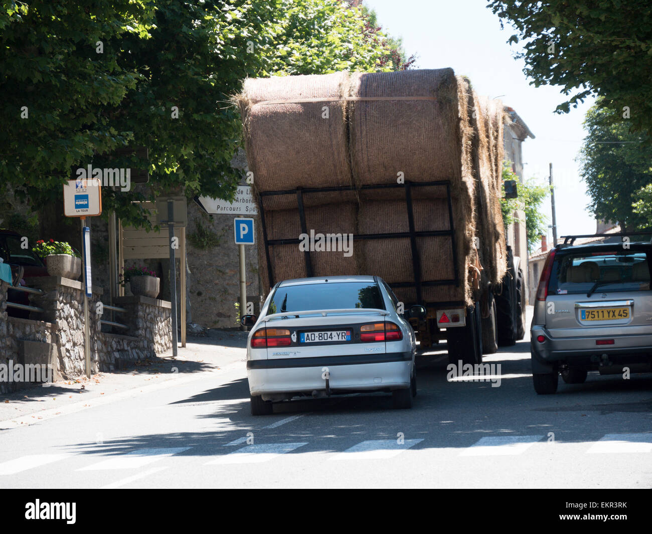 A car follows a farm tractor loaded with stray bales through a village ...