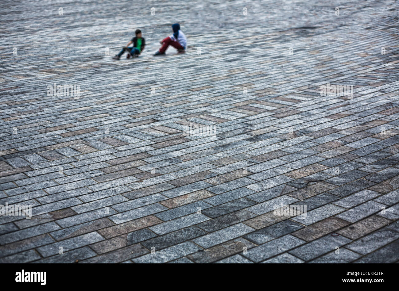 Two boys sitting over their skateboard on a square pavement, Spain ...