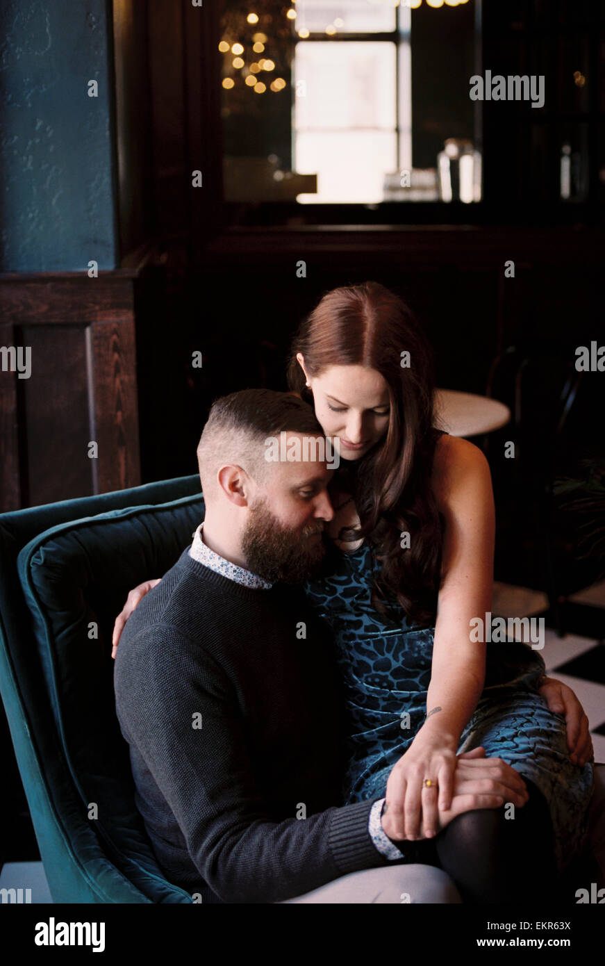 A couple on a date, a woman embracing a man seated in a chair Stock ...