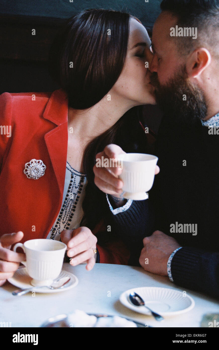 A couple seated side by side at a cafe table, kissing Stock Photo - Alamy