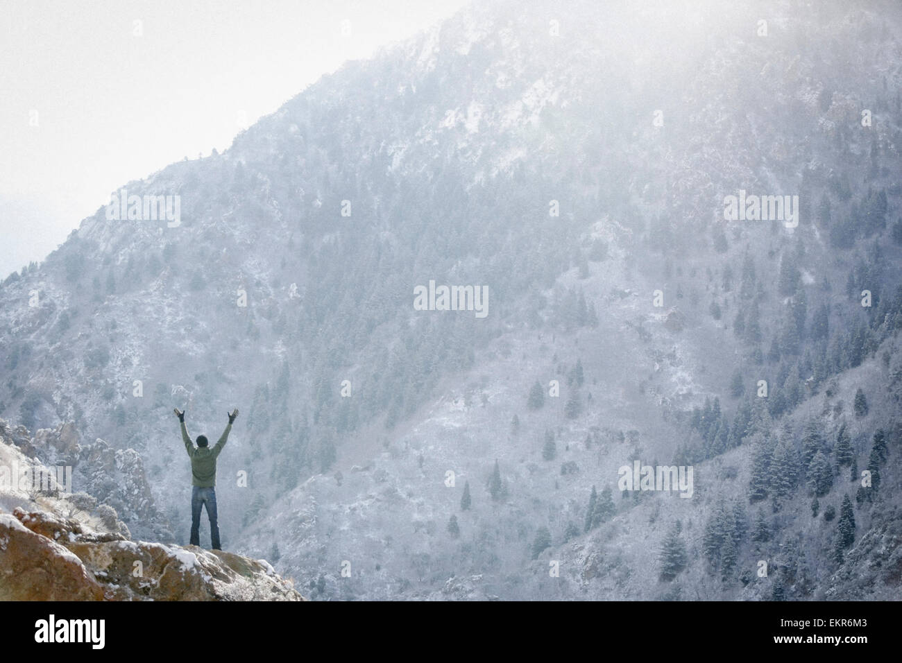 A man greeting the sun, with his arms raised on a rock outcrop in the ...