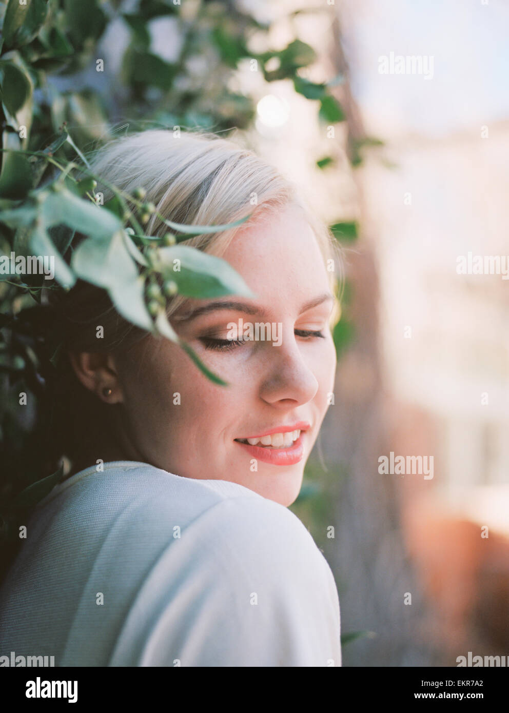 A pretty woman with a half smile, leaning against a vine growing up a ...