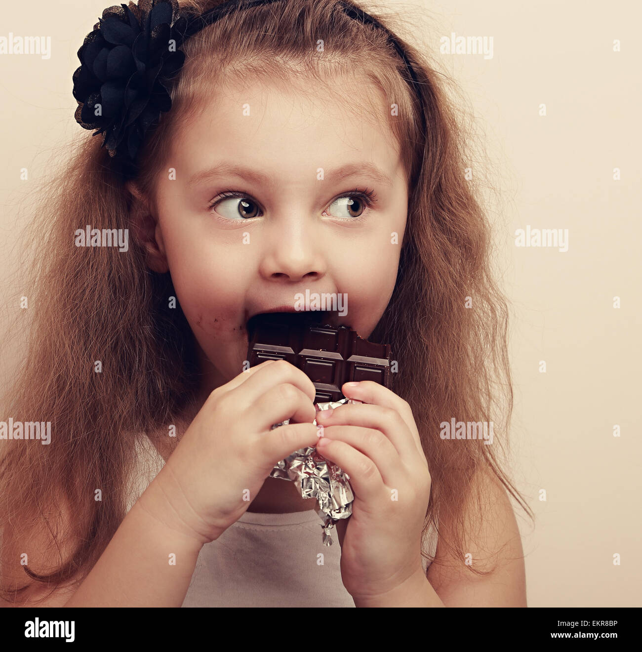 Happy surprising kid girl eating chocolate and looking with long hair ...