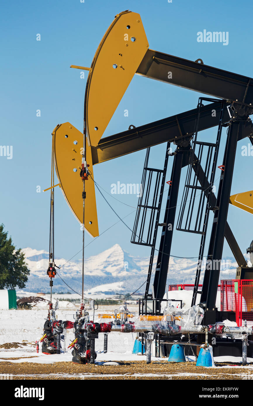 Pump jacks in a snow covered field with snow covered mountains and blue ...